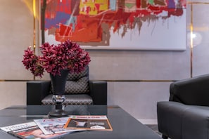 Um hall moderno com um sofá de couro preto, uma mesa de centro de vidro com revistas e um vaso de flores.