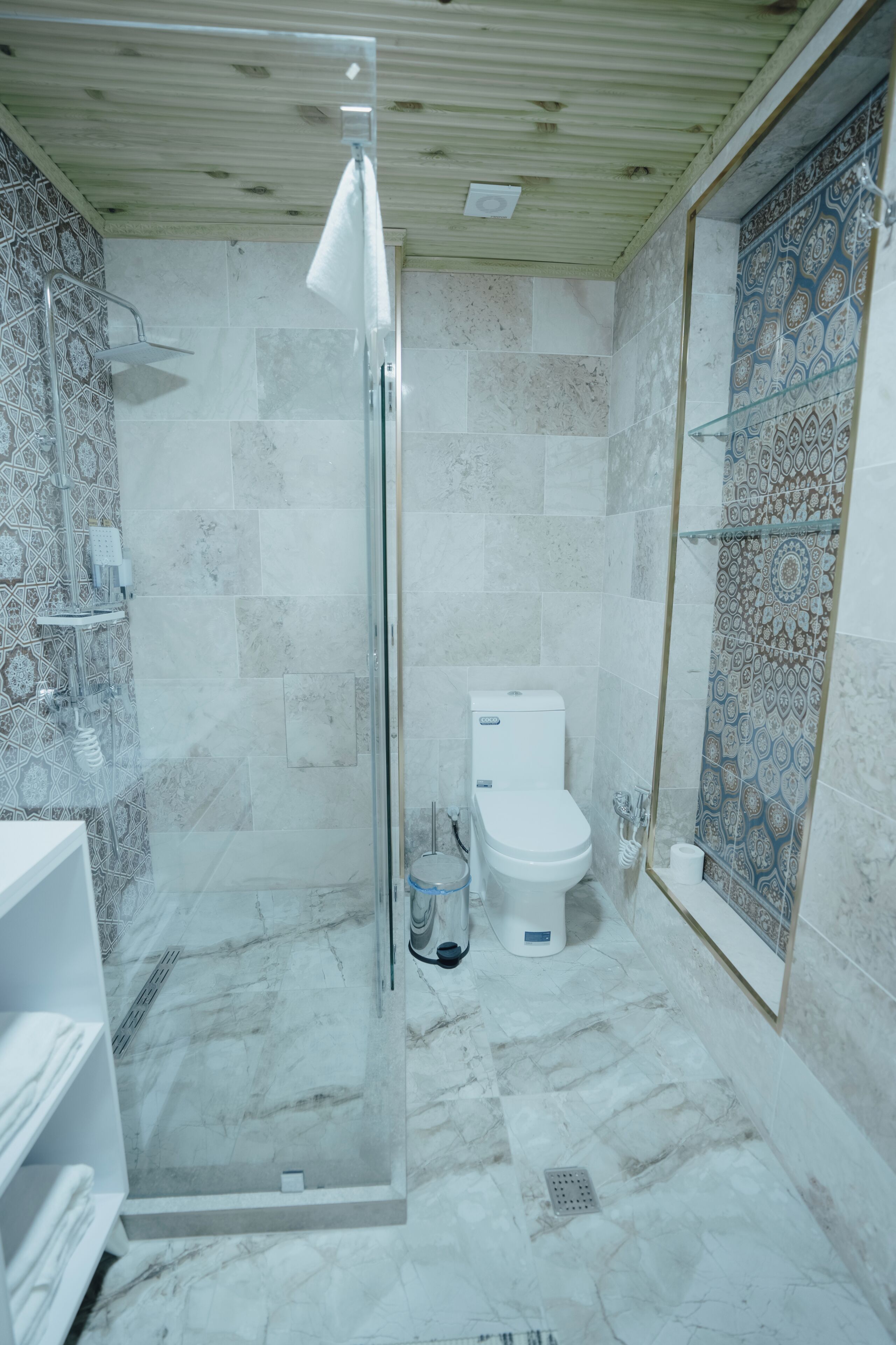 Casa de banho com cabine de duche em vidro, sanita e azulejos estampados nas paredes e no chão.