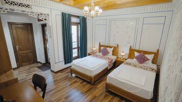 Quarto tradicional com duas camas de madeira, uma escrivaninha de madeira e um candelabro.