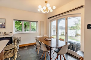 Uma sala de jantar com uma mesa grande, cadeiras, um lustre e janelas amplas com vista para o exterior.