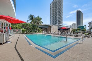 Piscina com espreguiçadeiras e guarda-sóis, cercada por edifícios altos.