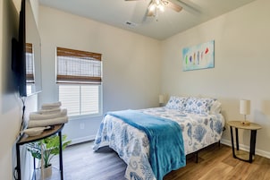 Quarto com cama, mesa de cabeceira, abajur, janela com persianas, ventilador de teto e um quadro na parede.