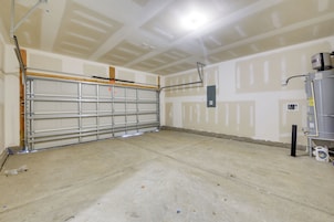 Uma garagem com porta metálica fechada, aquecedor de água e chão de concreto.