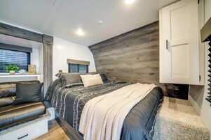 Quarto compacto com cama, sofá e janela.