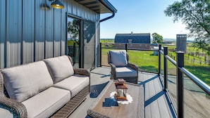 Um deck com mobiliário de vime e um candeeiro, com vista para uma paisagem rural.