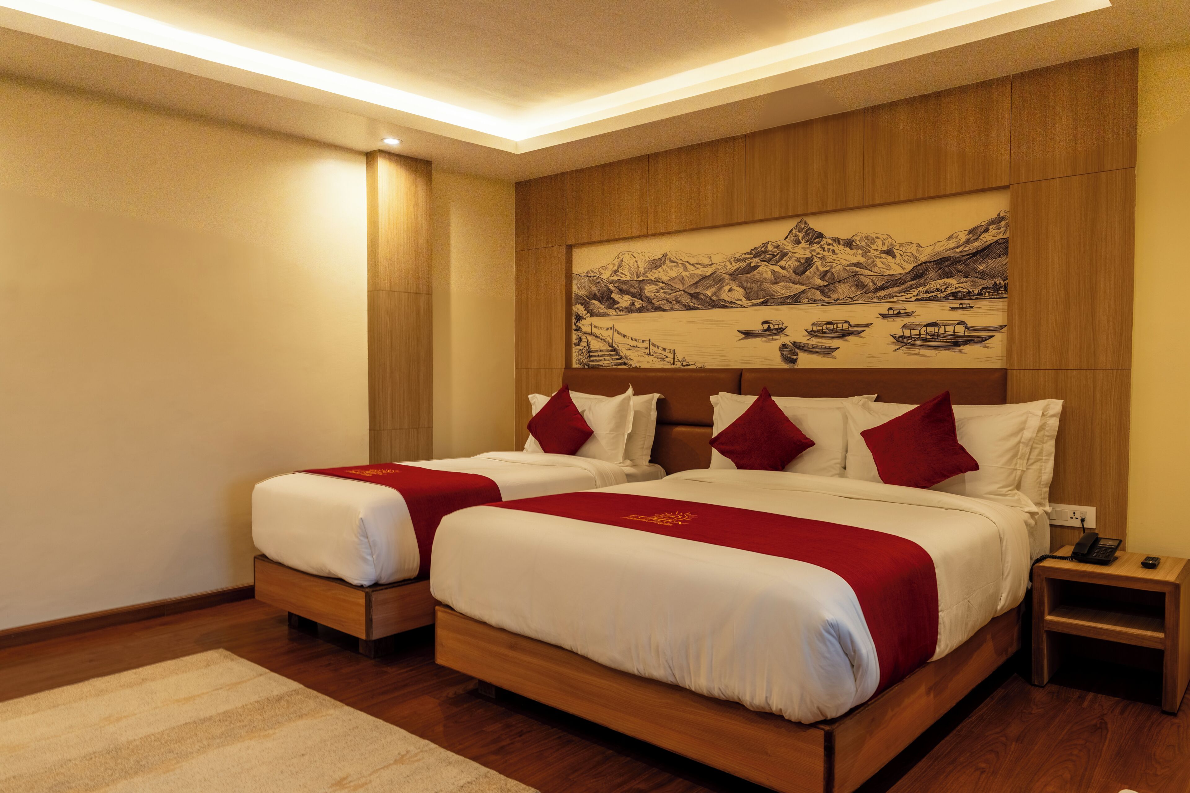 Quarto de hotel com duas camas, cabeceira de madeira, pintura de montanhas e uma pequena mesa de cabeceira com telefone.
