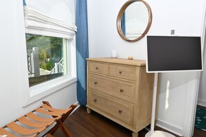 Quarto com cômoda de madeira, um banco, janela com vista, espelho e televisão de tela plana.