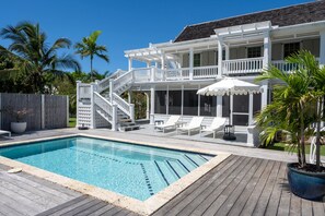 Uma casa de dois andares com piscina, área de estar ao ar livre e varanda coberta.