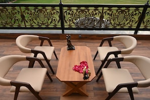 Uma mesa de madeira com quatro cadeiras, uma estátua e um arranjo de flores vermelhas em formato de coração numa varanda com guarda-corpo decorativo.