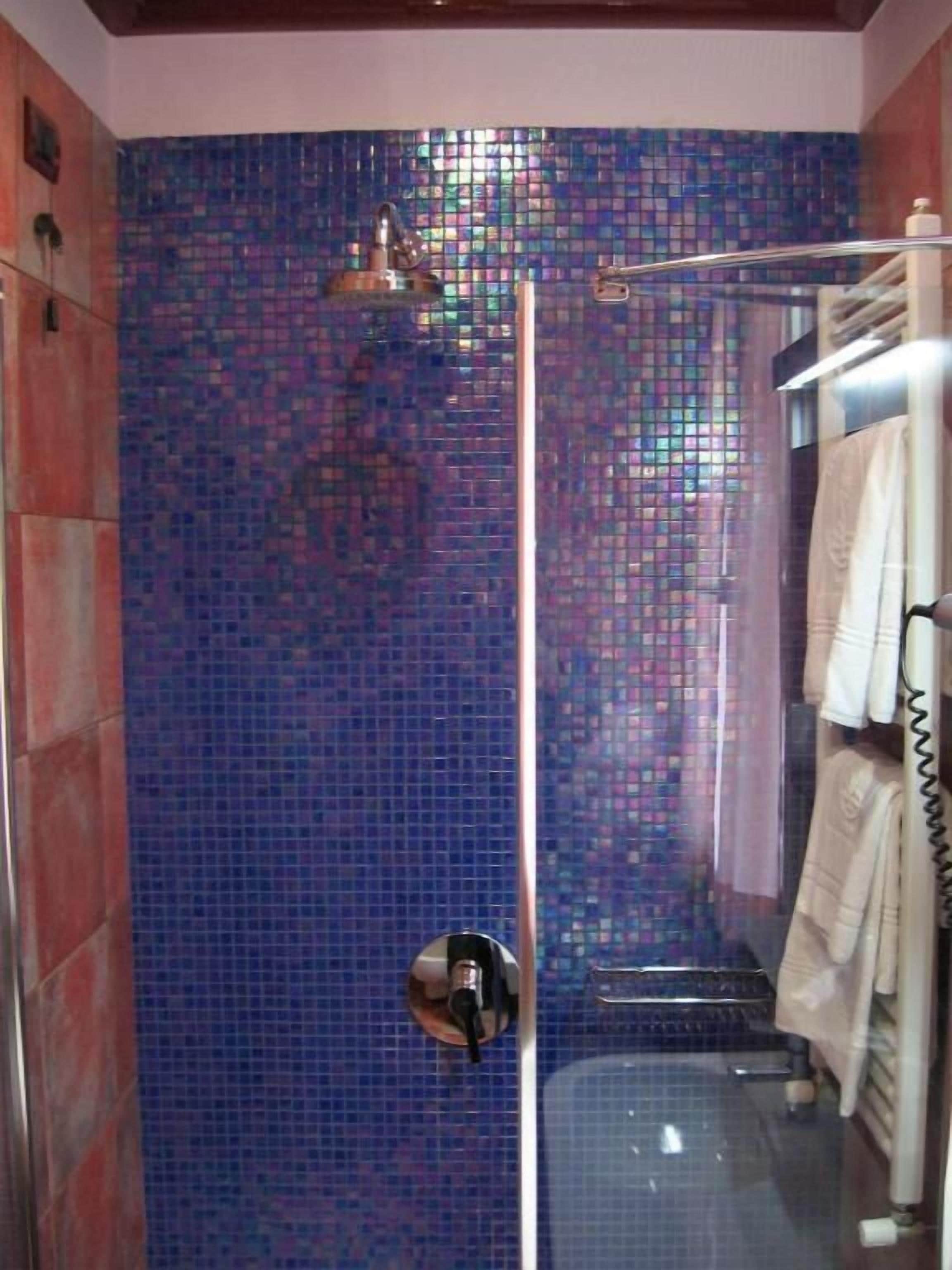 Um chuveiro com porta de vidro e parede revestida de azulejos.