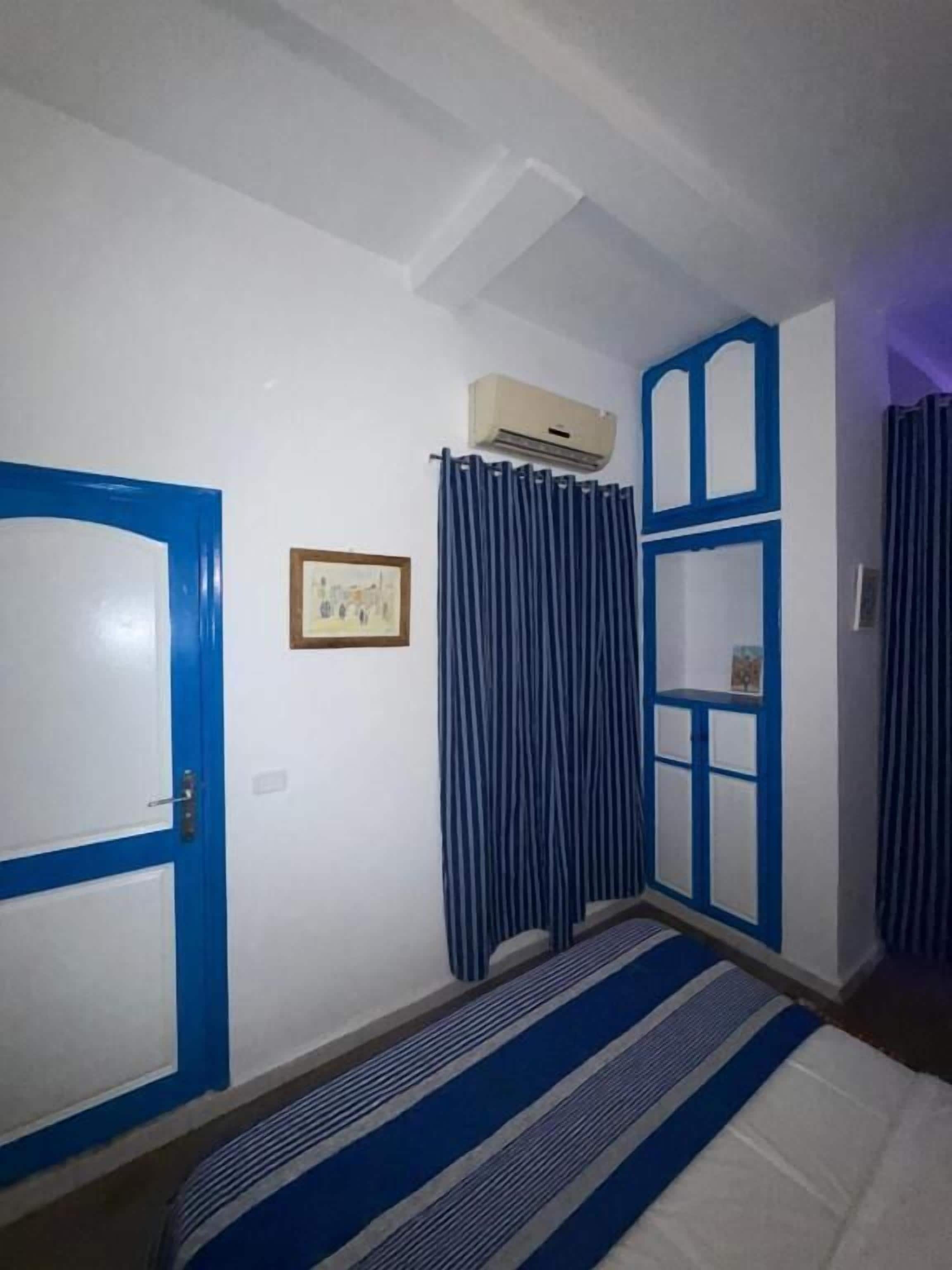 Quarto com cama, porta, aparelho de ar condicionado e cortina.