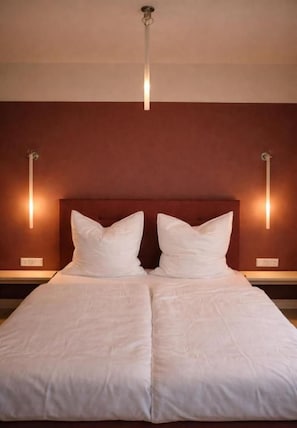 Uma cama de casal com cabeceira de madeira, duas mesas de cabeceira e luminárias fixadas na parede.