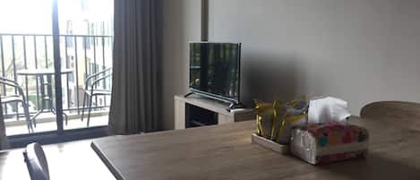 Quarto de hotel com mesa de madeira, televisão em móvel, janela com cortinas e vista para a varanda externa.