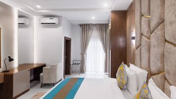 Quarto de hotel moderno com cama, mesa de cabeceira, abajur e vista para o corredor.