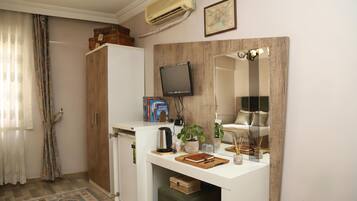 Quarto de hotel com guarda-roupa de madeira, secretária branca com chaleira, televisão e um espelho grande.