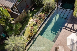 Piscina com deck de madeira, rodeada por vegetação exuberante e um caminho de pedra.