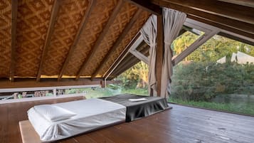 Quarto com teto de madeira, cama com colchão branco e vista para o verde lá fora.