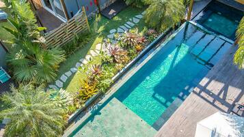 Piscina no terraço com deck de madeira, cercada por plantas tropicais e um pequeno jardim.