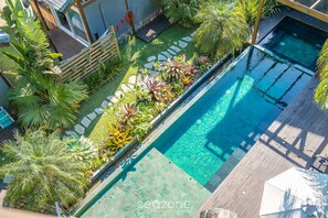 Piscina no terraço com deck de madeira, cercada por plantas tropicais e um pequeno jardim.
