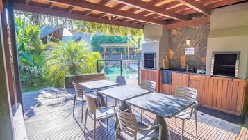 Um pátio externo com deck de madeira, mesas, cadeiras, espaço para churrasco e uma parede de pedra.