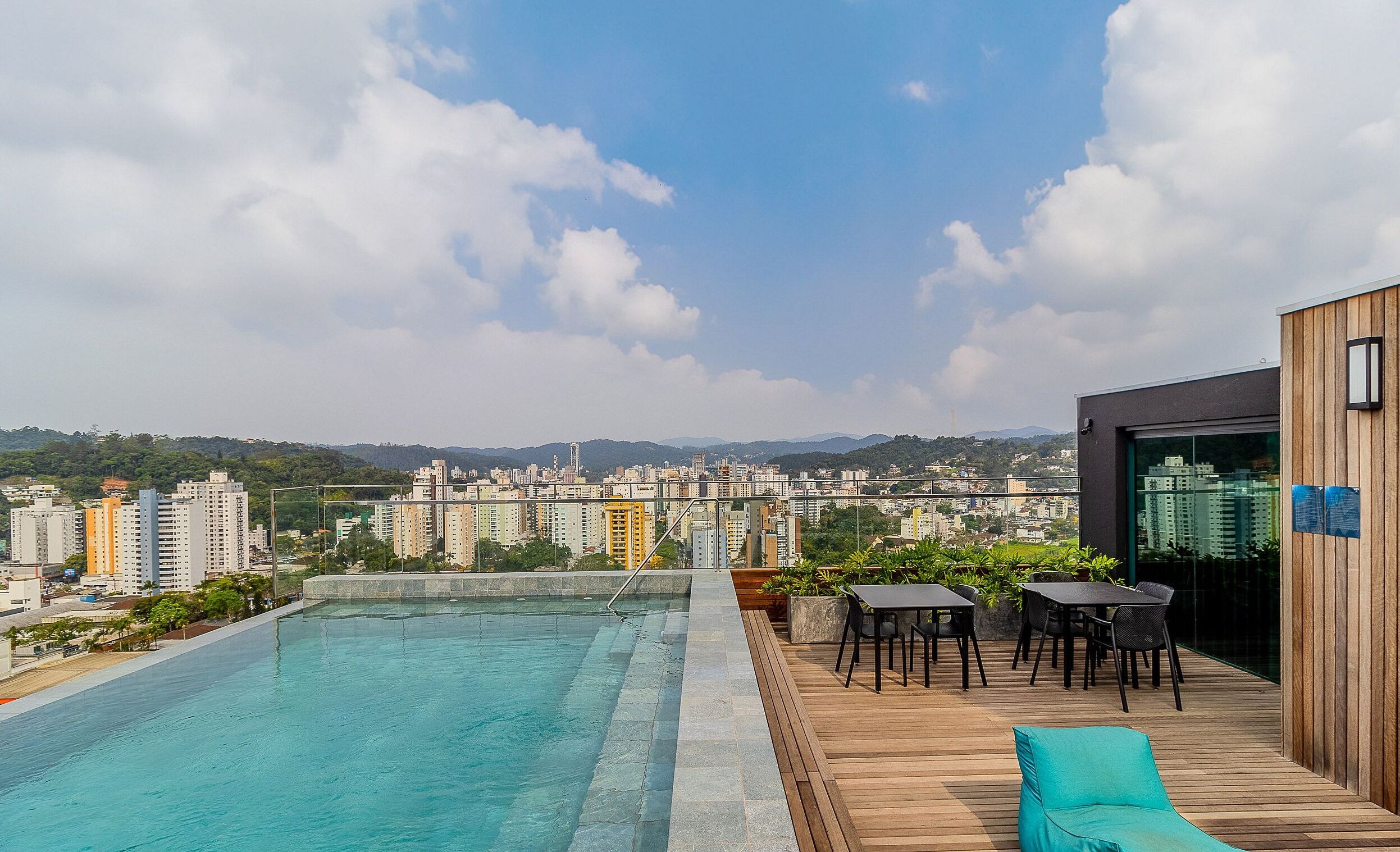 Piscina no terraço com vista para a paisagem urbana e montanhas.
