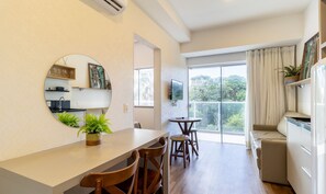 Cozinha moderna com área de refeições, espelho redondo e varanda com vista para árvores.