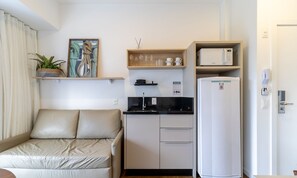 Um espaço compacto com cozinha compacta, sofá, geladeira e pequeno espaço para refeições.