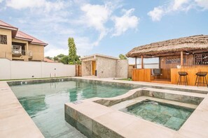 Piscina com hidromassagem, área de bar e um pequeno edifício com porta.