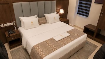 Quarto de hotel com uma cama grande, mesa de cabeceira, cadeira e um quadro na parede.