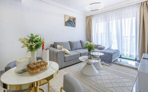 Uma sala de estar moderna com um sofá cinza, uma mesa de centro redonda e uma mesa de jantar com um vaso de flores.