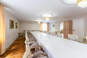 Uma longa mesa de banquete com cadeiras, um lustre e um guarda-roupa de madeira.