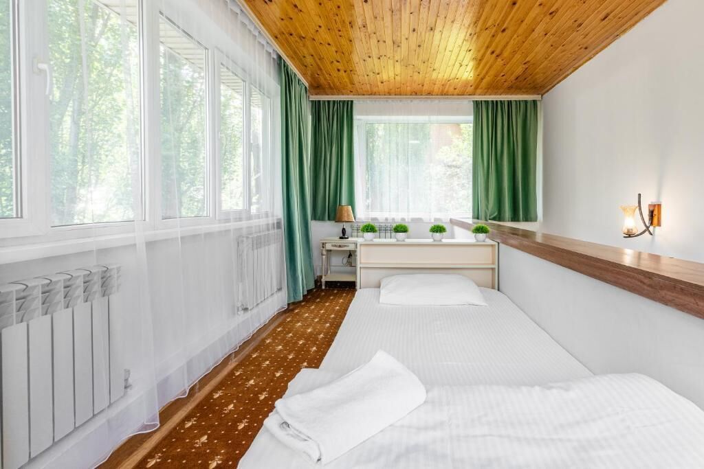 Quarto com duas camas, janela com cortinas, radiador e teto de madeira.