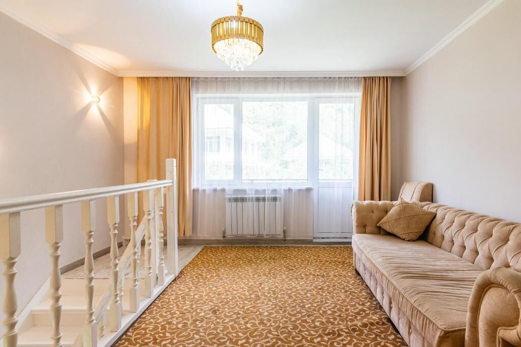 Um quarto com carpete estampado, um sofá, um candelabro e uma janela com cortinas.
