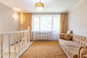 Um quarto com carpete estampado, um sofá, um candelabro e uma janela com cortinas.