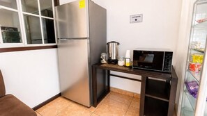 Cozinha compacta com geladeira, micro-ondas e uma pequena mesa com cafeteira e jarra de leite.