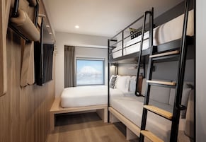 Quarto com beliche, vista para a montanha pela janela, cama plana e televisão fixada na parede.