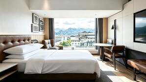 Quarto de hotel moderno com uma cama grande, uma escrivaninha, uma cadeira e vista para montanhas.