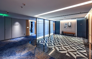 Um corredor moderno com piso estampado em padrão geométrico, um banco e parede com quadros emoldurados.