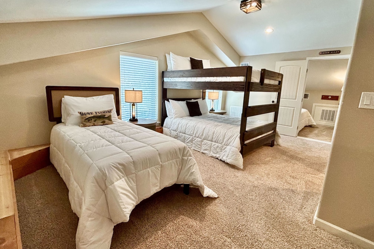 Quarto com duas camas beliche, uma mesinha de cabeceira com abajur e uma janela com persianas.
