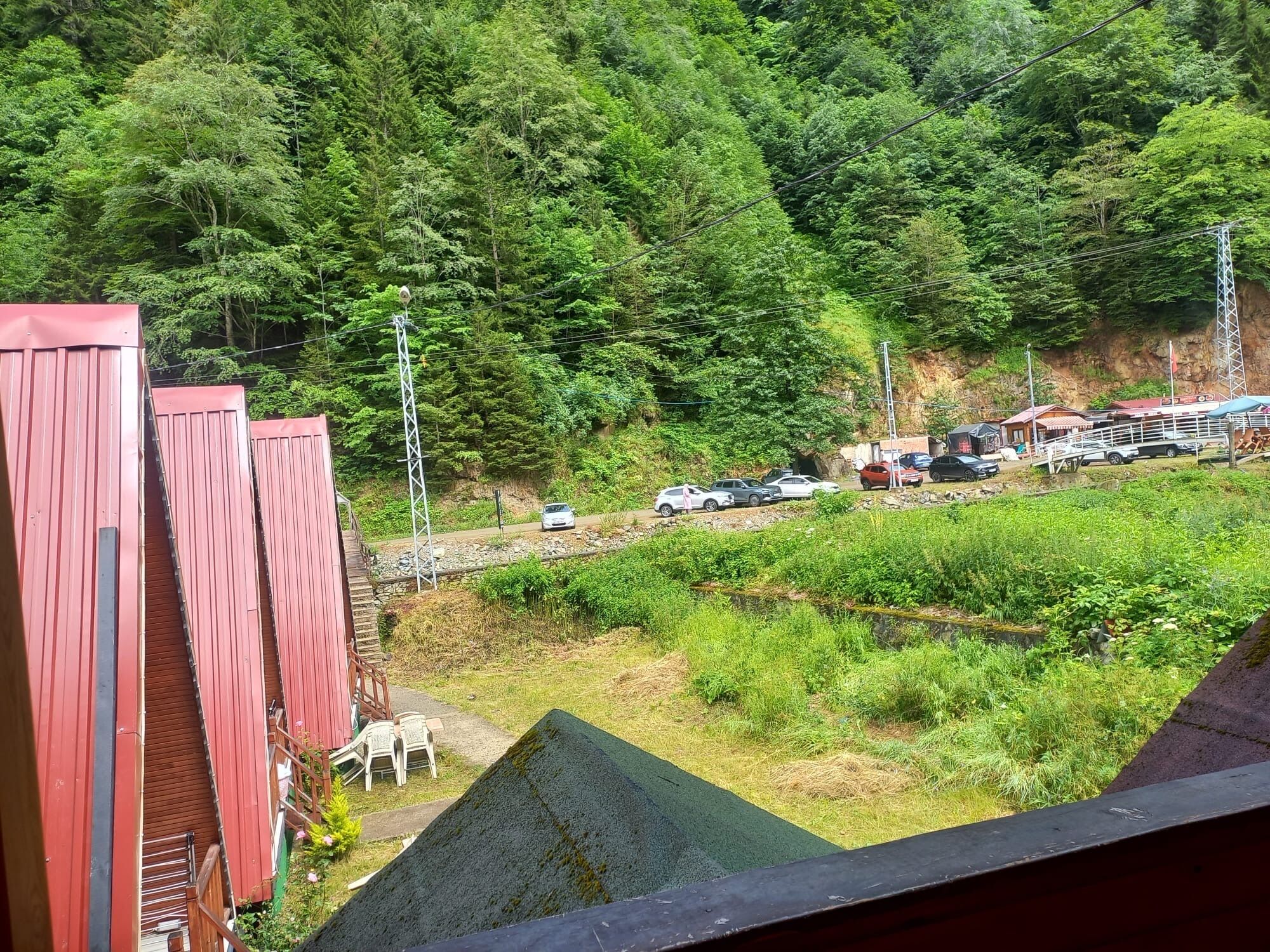 Vista de uma área de estacionamento com vários carros, cercada por vegetação exuberante e um edifício vermelho.