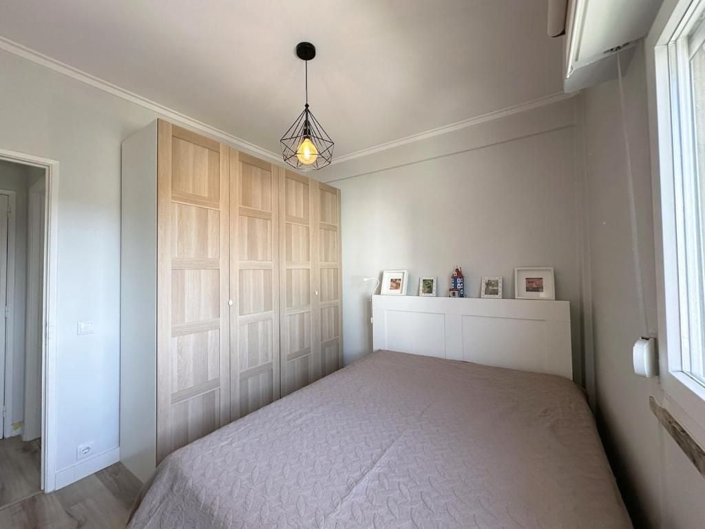 Quarto com cama, guarda-roupa, luz pendente e janela.