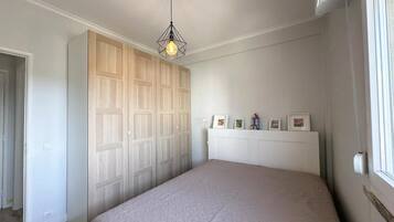 Quarto com cama, guarda-roupa, luz pendente e janela.