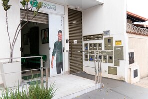 Entrada de um edifício com uma porta verde, uma câmera de segurança e vários caixas de correio numerados na parede.
