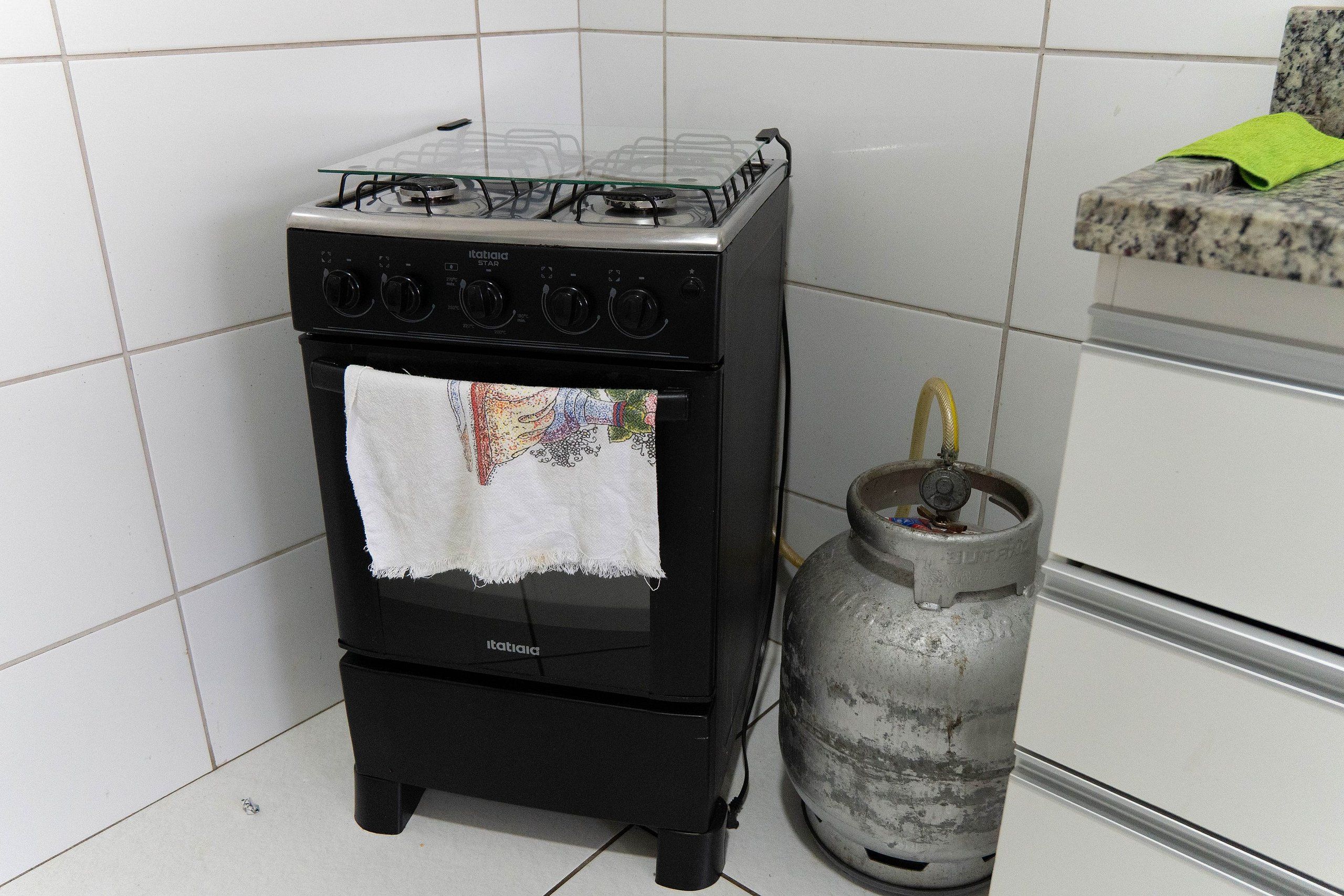 Cozinha compacta com fogão preto, cilindro de gás e painel de azulejos.