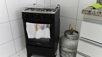 Cozinha compacta com fogão preto, cilindro de gás e painel de azulejos.