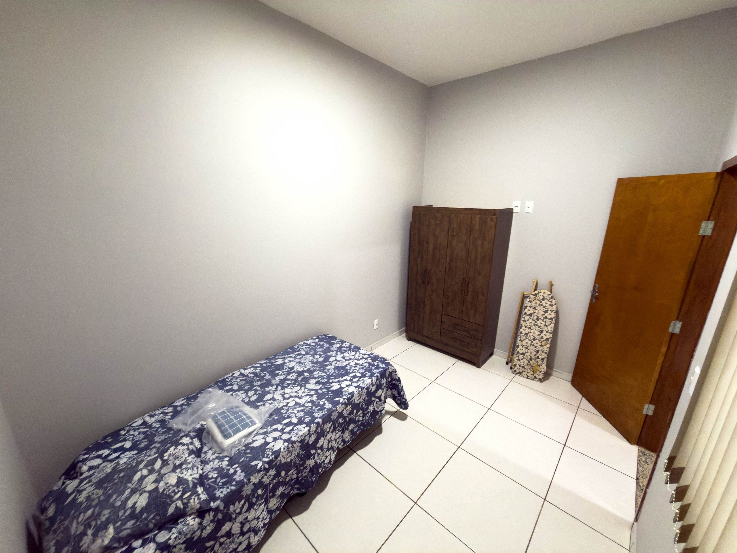 Quarto com uma cama de solteiro, um guarda-roupa e uma porta.