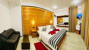 Quarto de hotel moderno com cabeceira de madeira, cama com roupa de cama listrada, manta vermelha, sofá preto e televisão de tela plana.