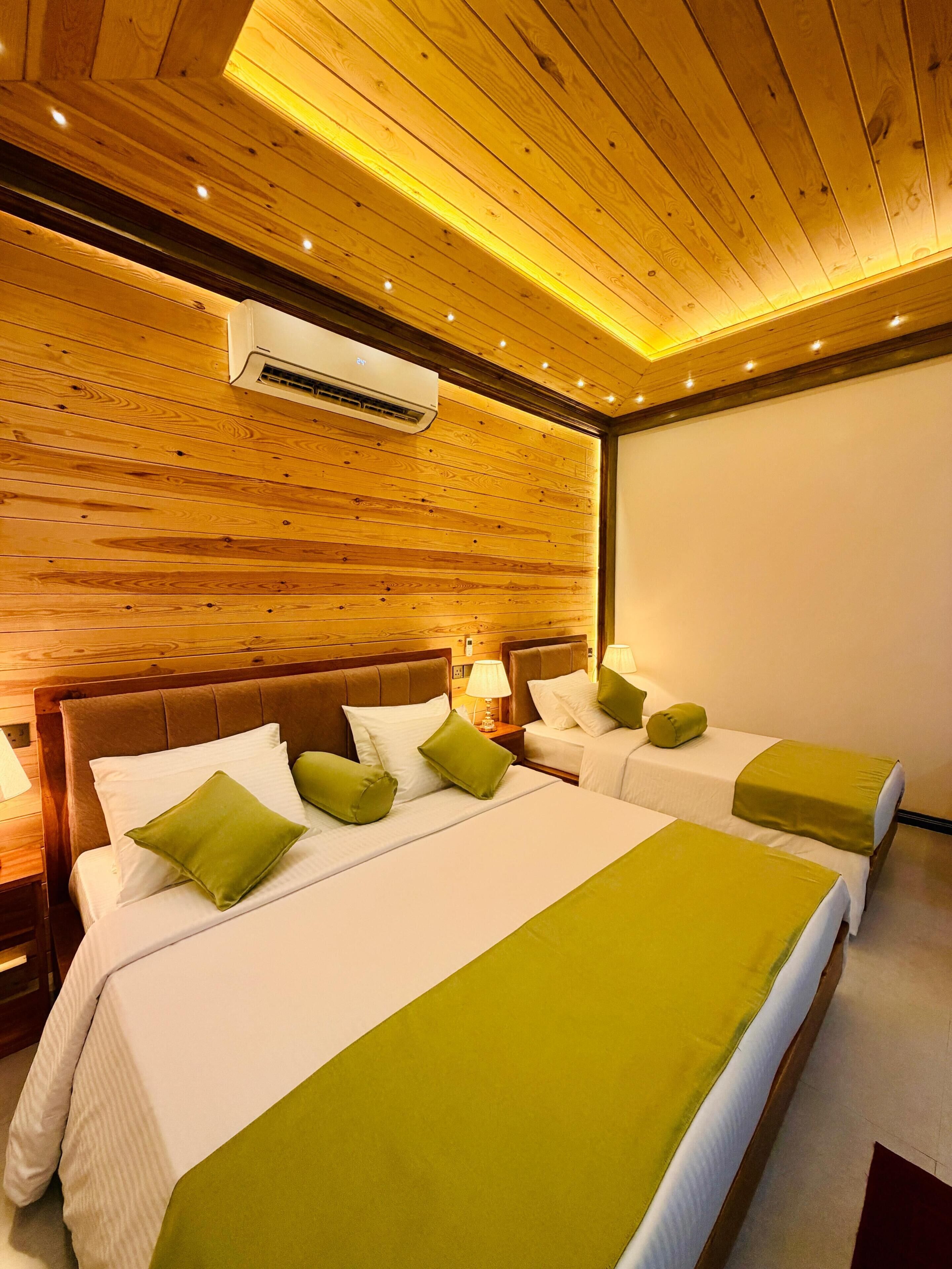 Quarto de hotel com duas camas, painéis de madeira nas paredes e um aparelho de ar condicionado.