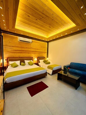 Quarto de hotel moderno com duas camas, um sofá, uma mesa de centro e um tapete vermelho.