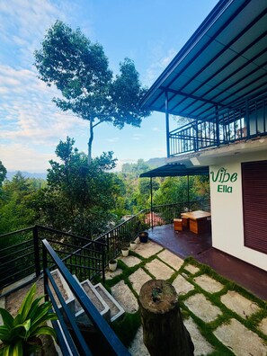 Uma área externa coberta com um banco de madeira, uma escada e uma placa com a inscrição 'Vibe Ella'.